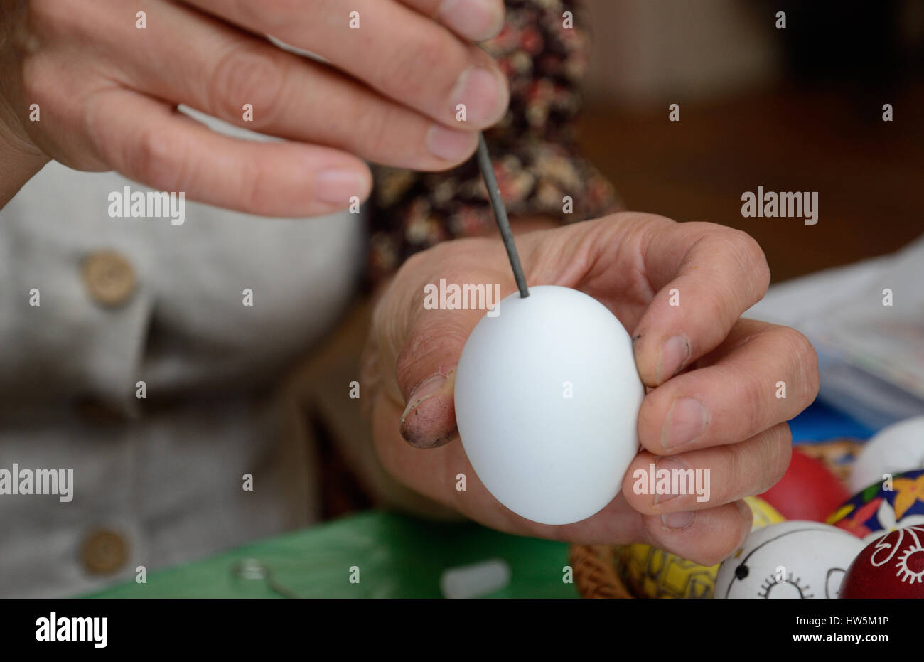 The human hands are perforating a white egg with a round needle file ...