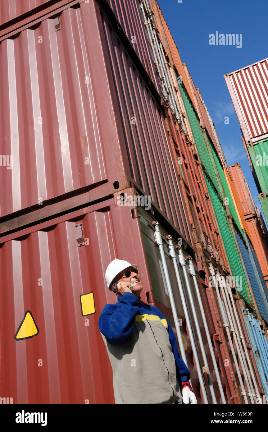 MODEL RELEASED. Industrial worker on cell phone with cargo containers ...