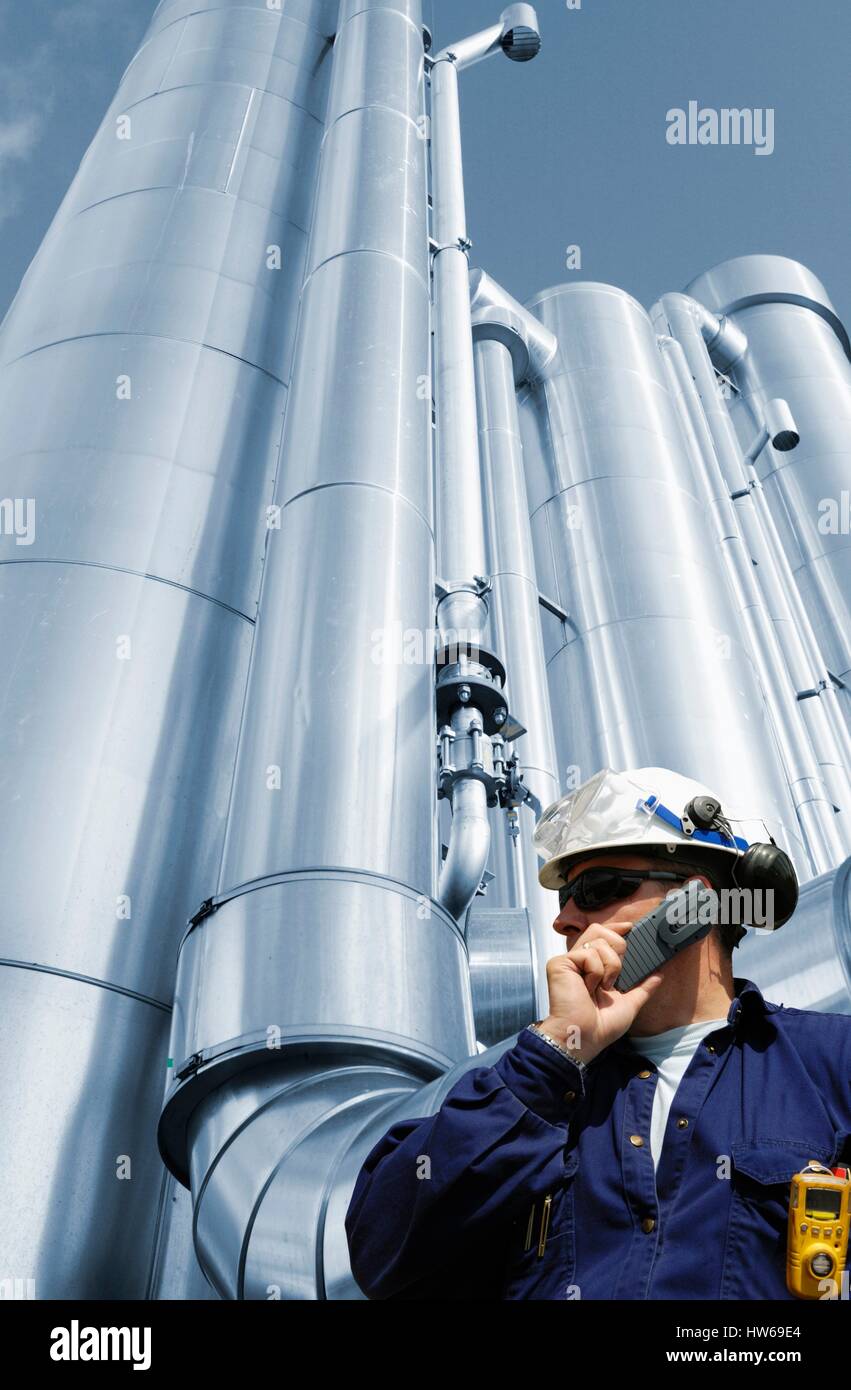 MODEL RELEASED. Oil refinery worker on cell phone with pipework in ...