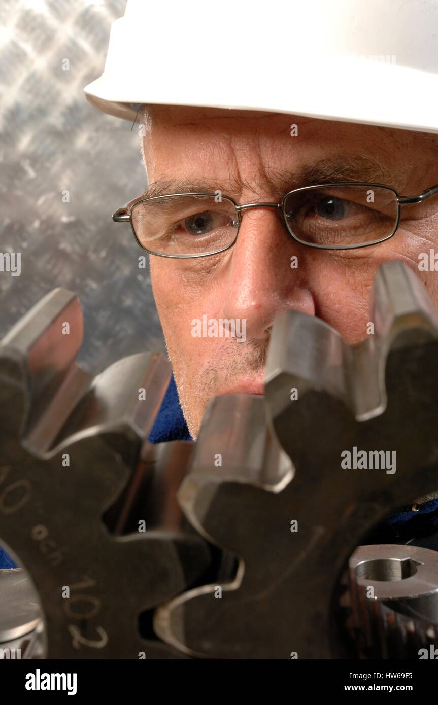 MODEL RELEASED. Engineer scrutinising metal cogs Stock Photo - Alamy