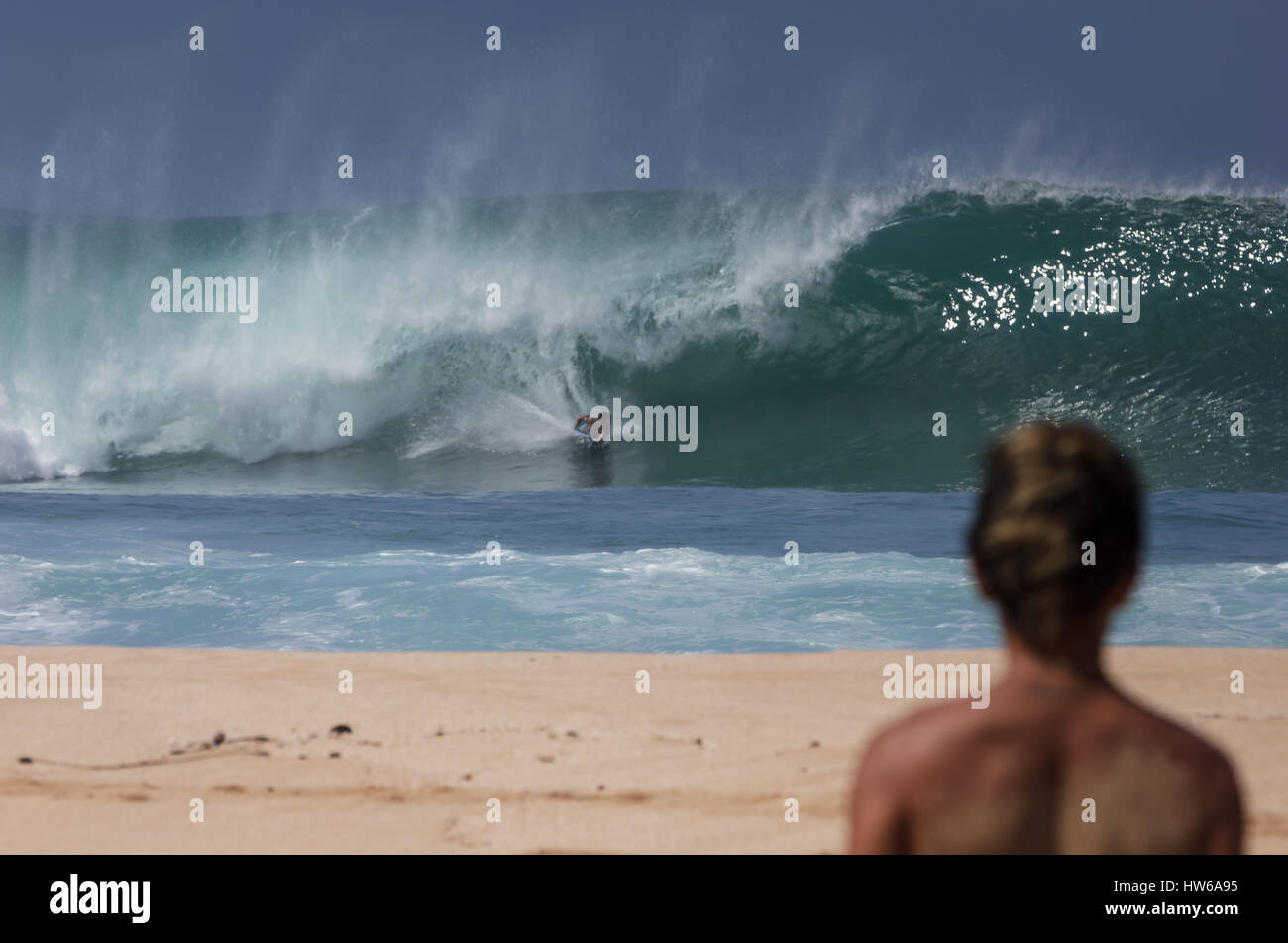 A young man watches a surfer catching a big Ocean wave at world famous ...