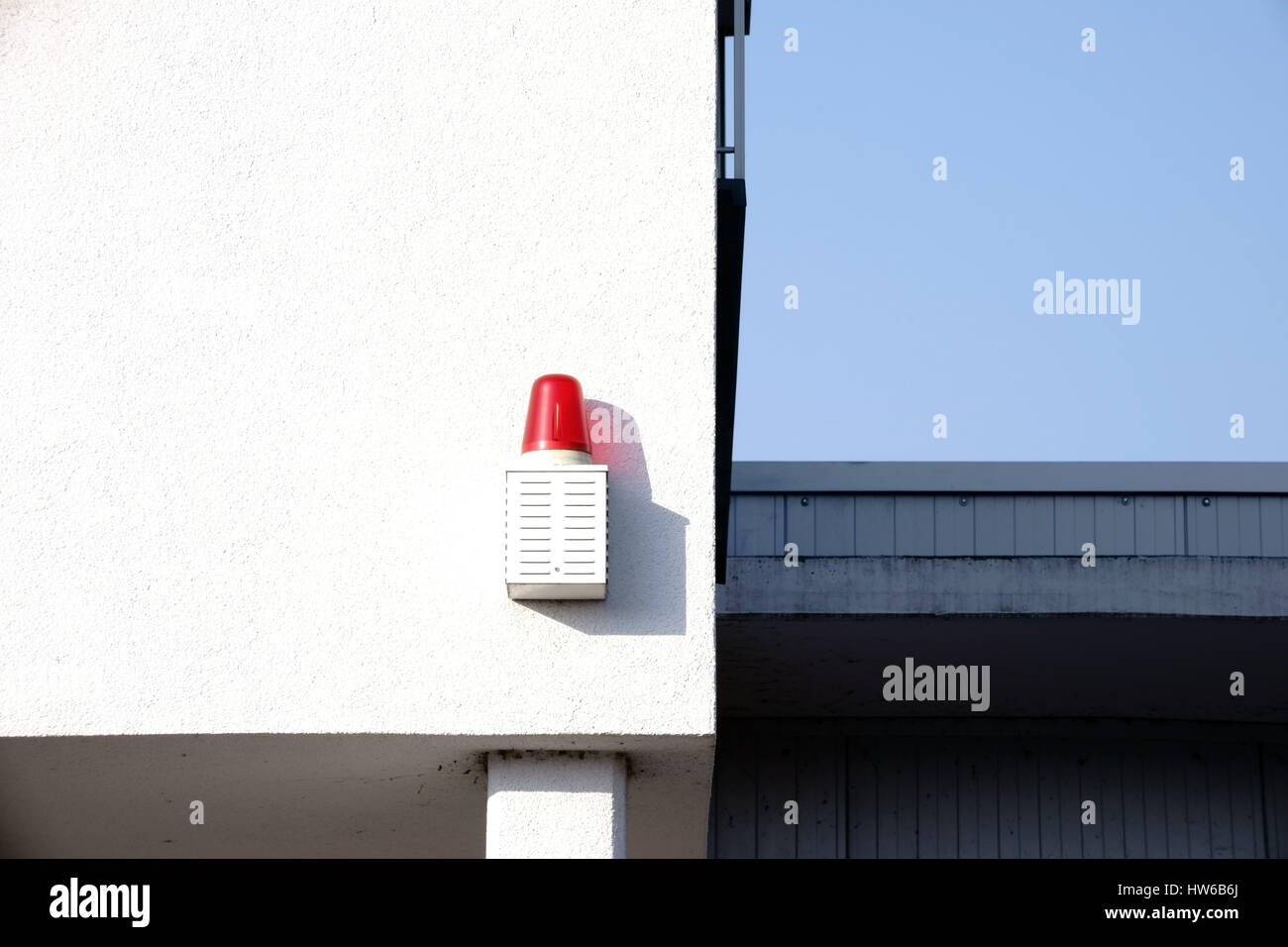 A red warning light with a speaker throws a shadow on a white wall ...