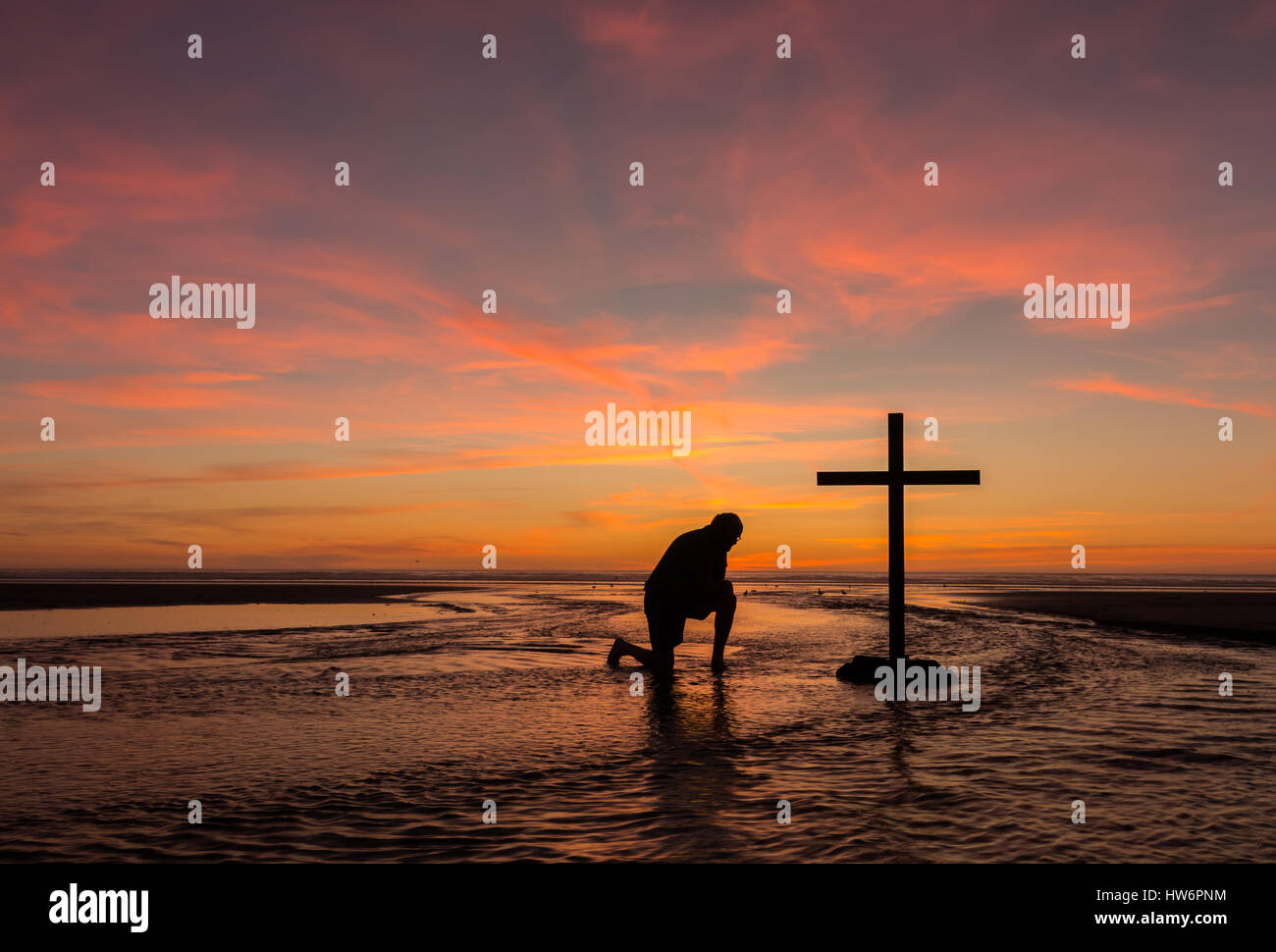 A man praying by a black cross with a flowing stream water around it ...