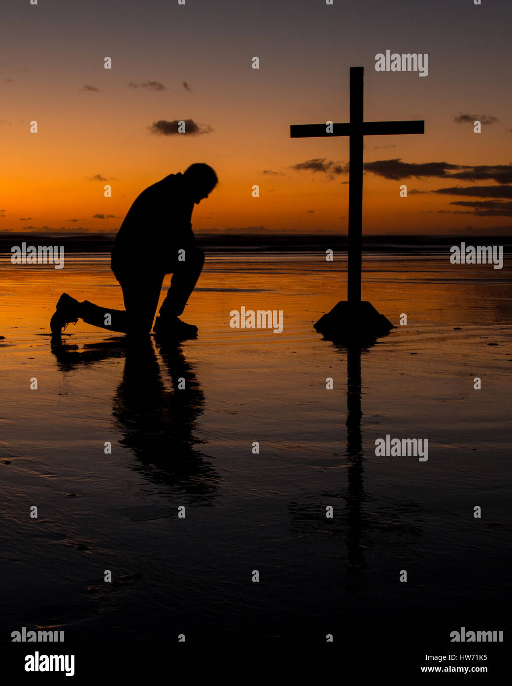 Cross with a man kneel in prayer on a beach at sunset Stock Photo - Alamy