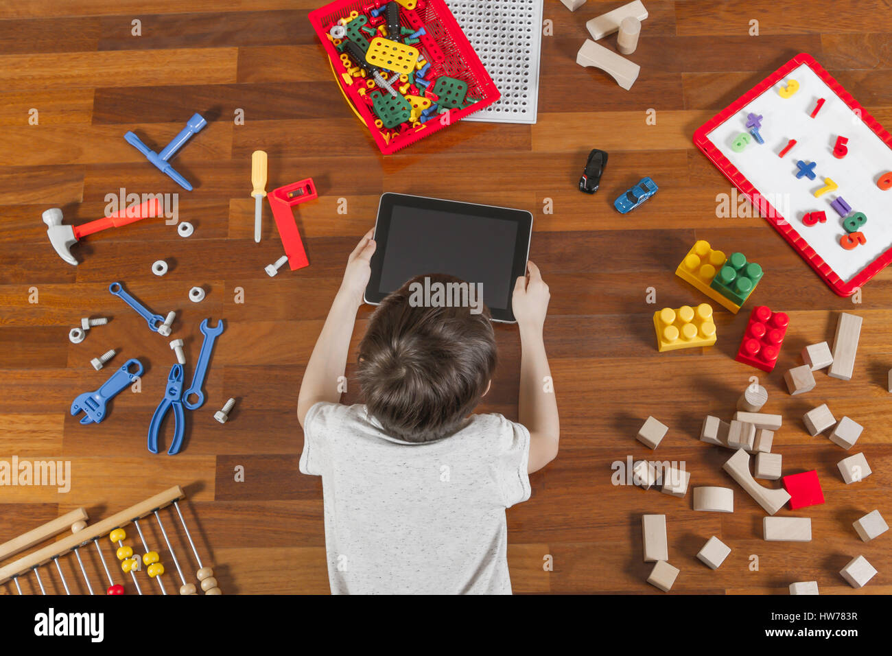 Little kid lying and playing with tablet computer. Lot of toys around ...