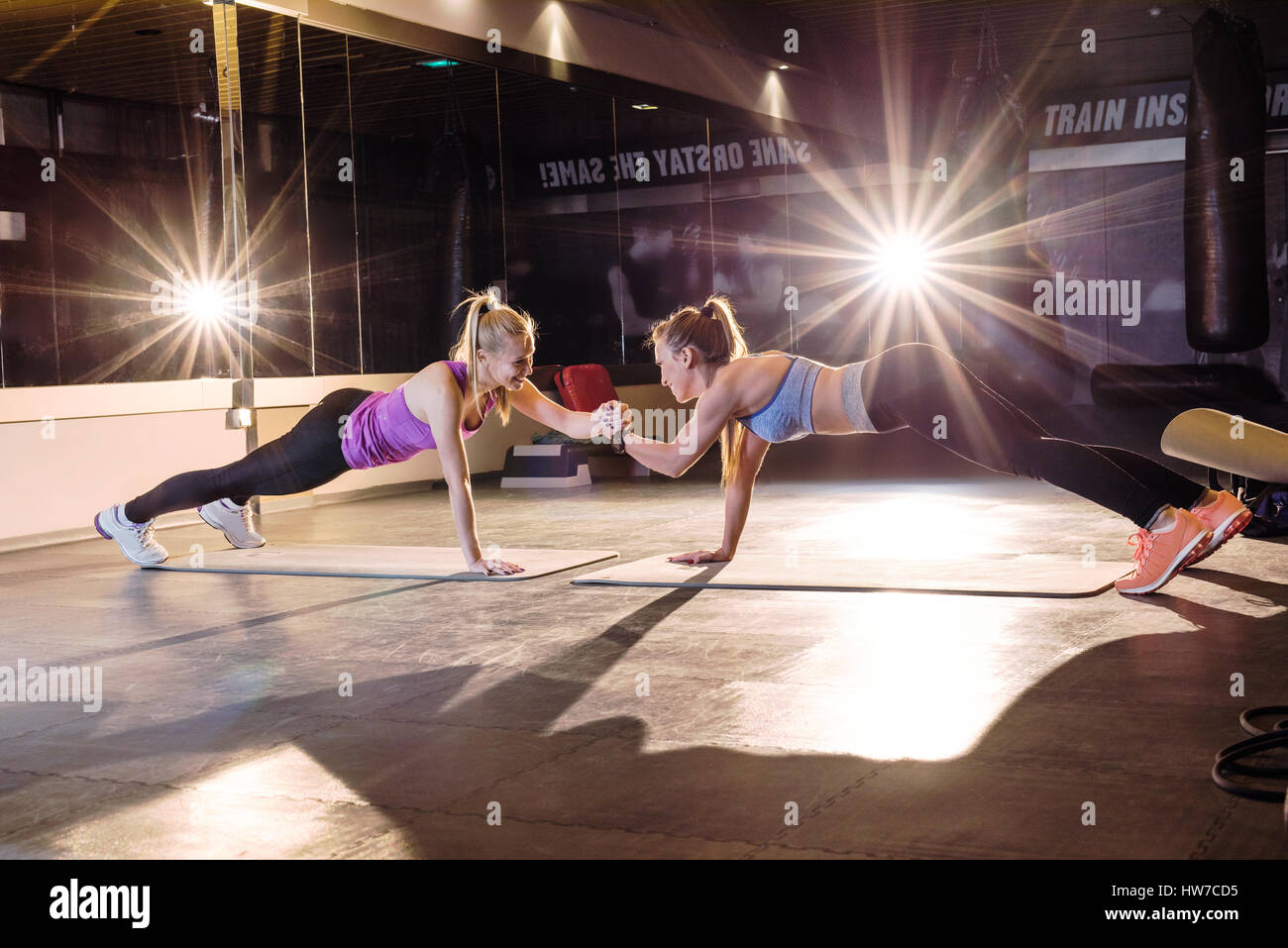 Two beautiful young athletic women doing push ups together. Hand shake ...