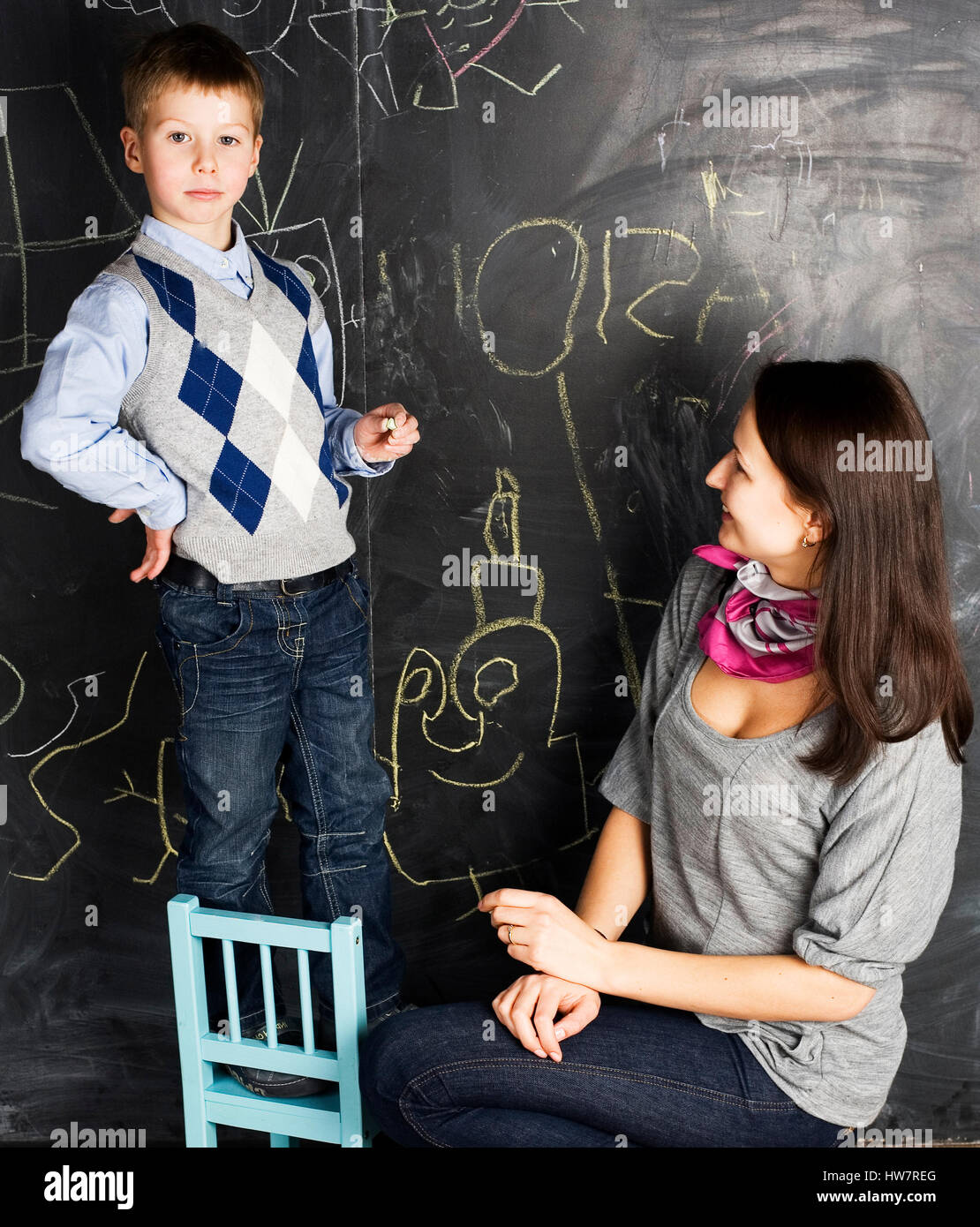 little cute boy with young teacher in classroom studying at blackboard ...