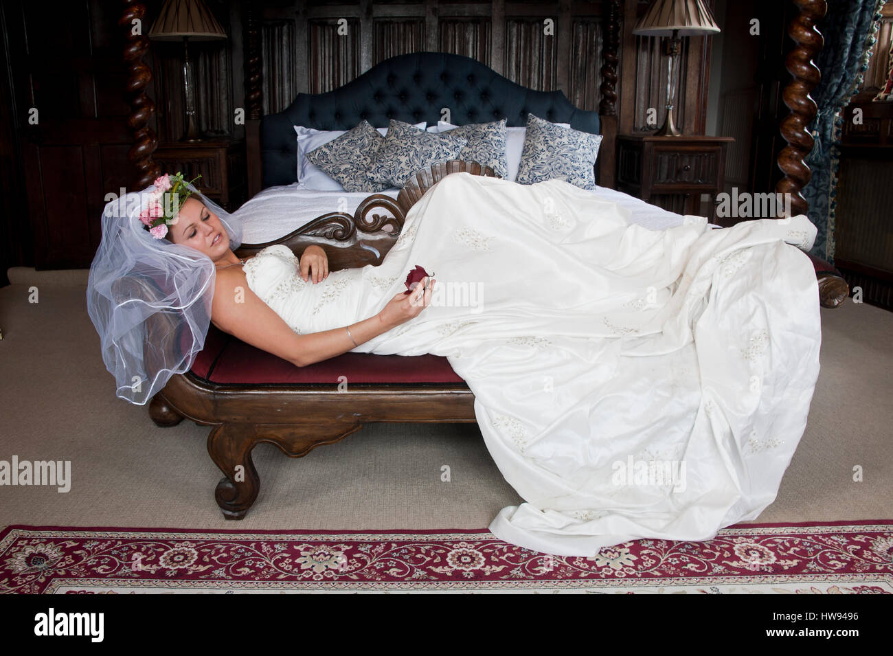 Young woman wearing a white wedding dress, reclining on a sofa, looking ...