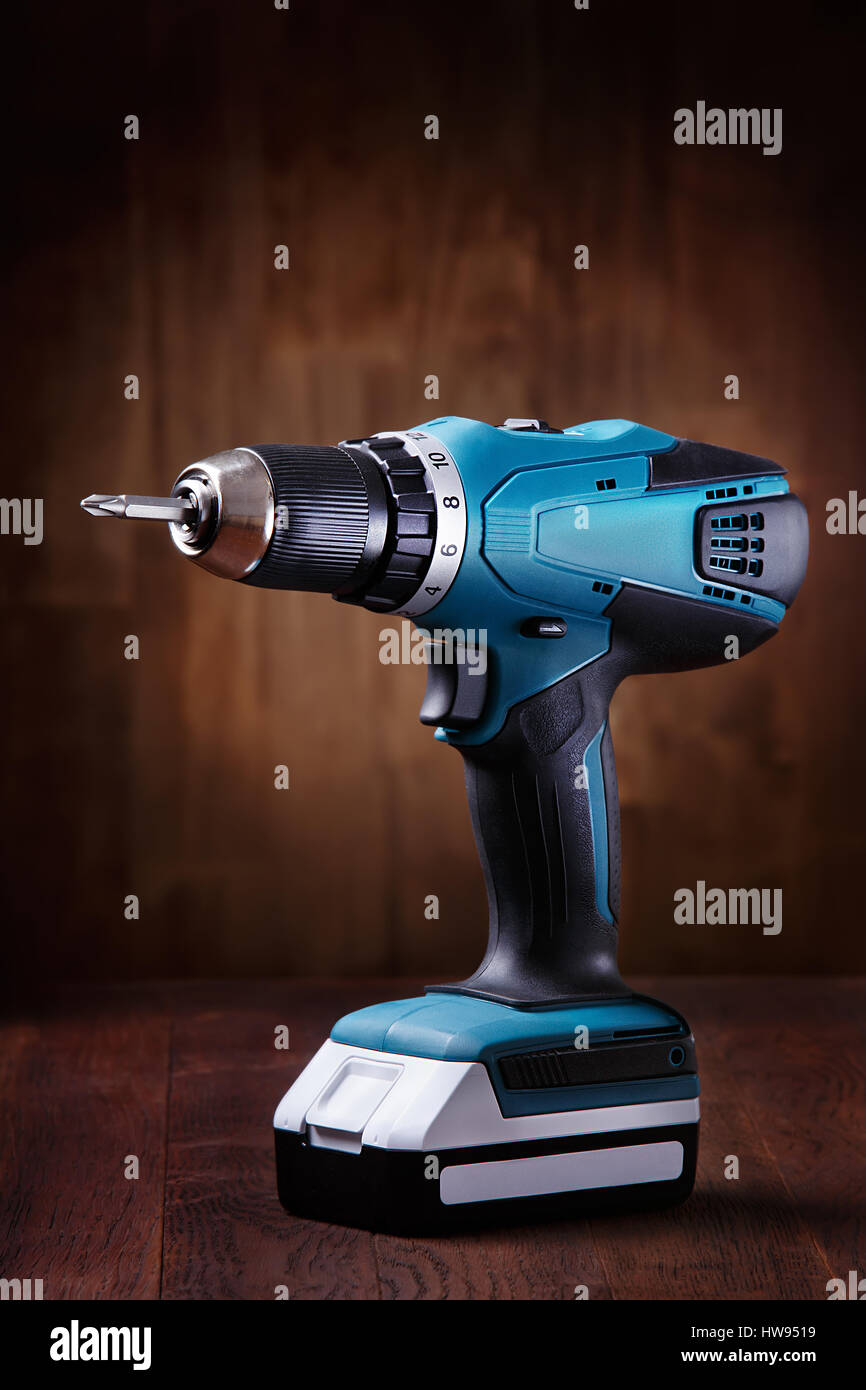 Blue cordless screwdriver with a drill on wooden table with wooden ...