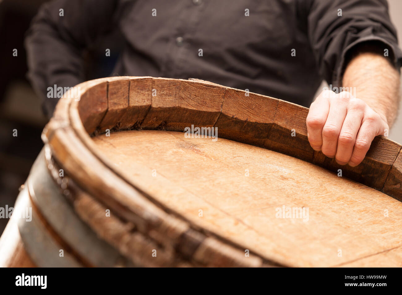 Man standing with his hand on a wooden oak barrel or cask in a winery ...