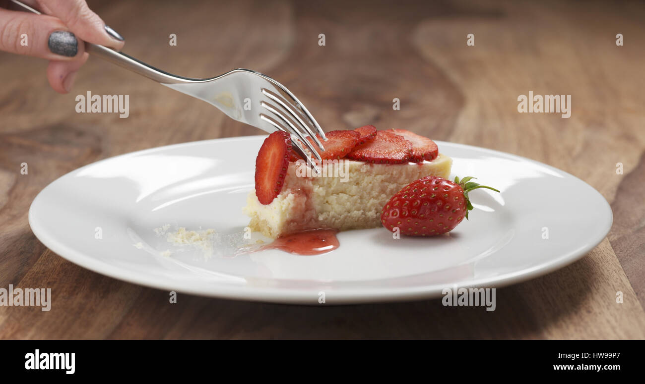 eating strawberry cheesecake with fork on wood table Stock Photo - Alamy