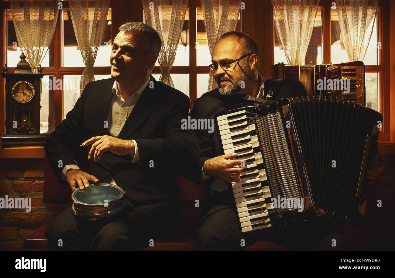 Portraits of percussionist and accordionist in front of a wooden window ...