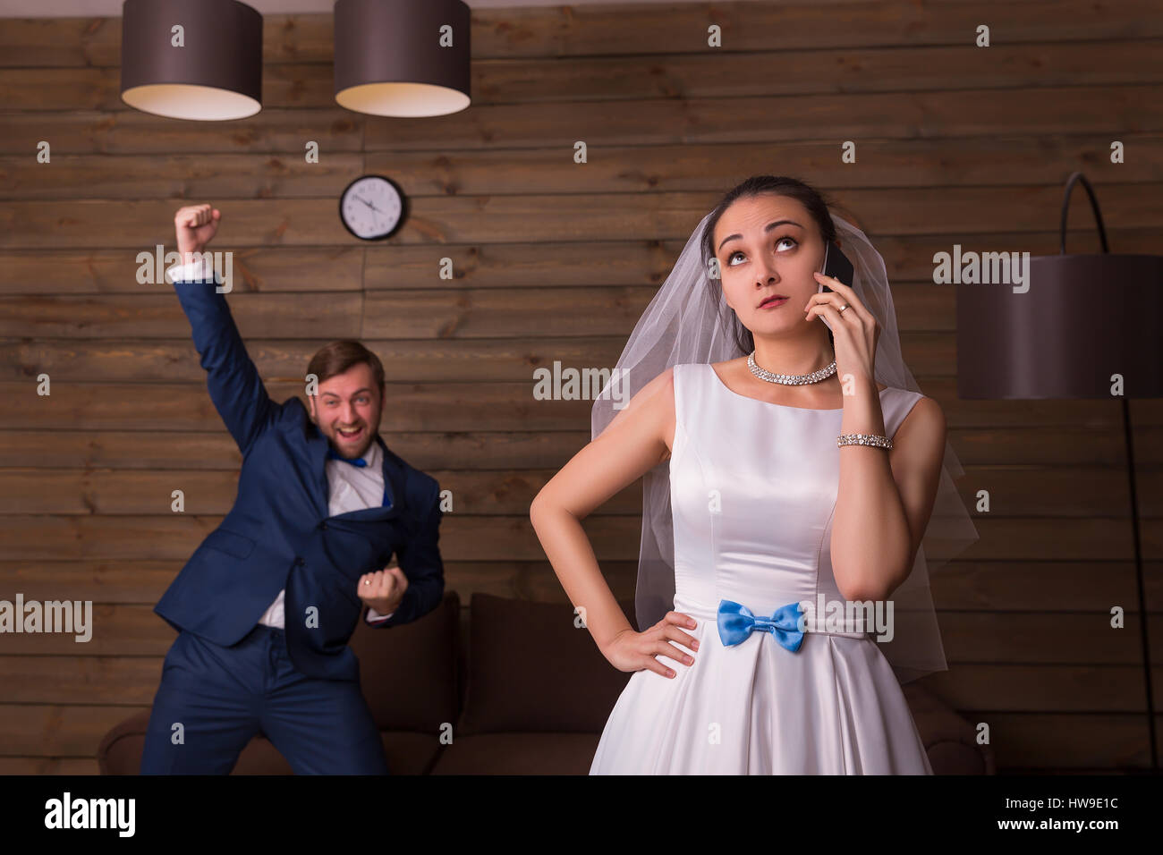 Portrait of bride with mobile phone against happy groom, wooden room on ...