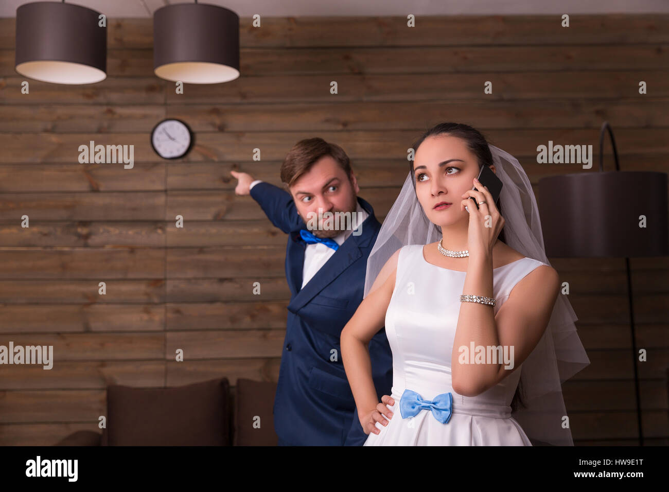 Portrait of bride talking by phone and dissatisfied groom showing on ...