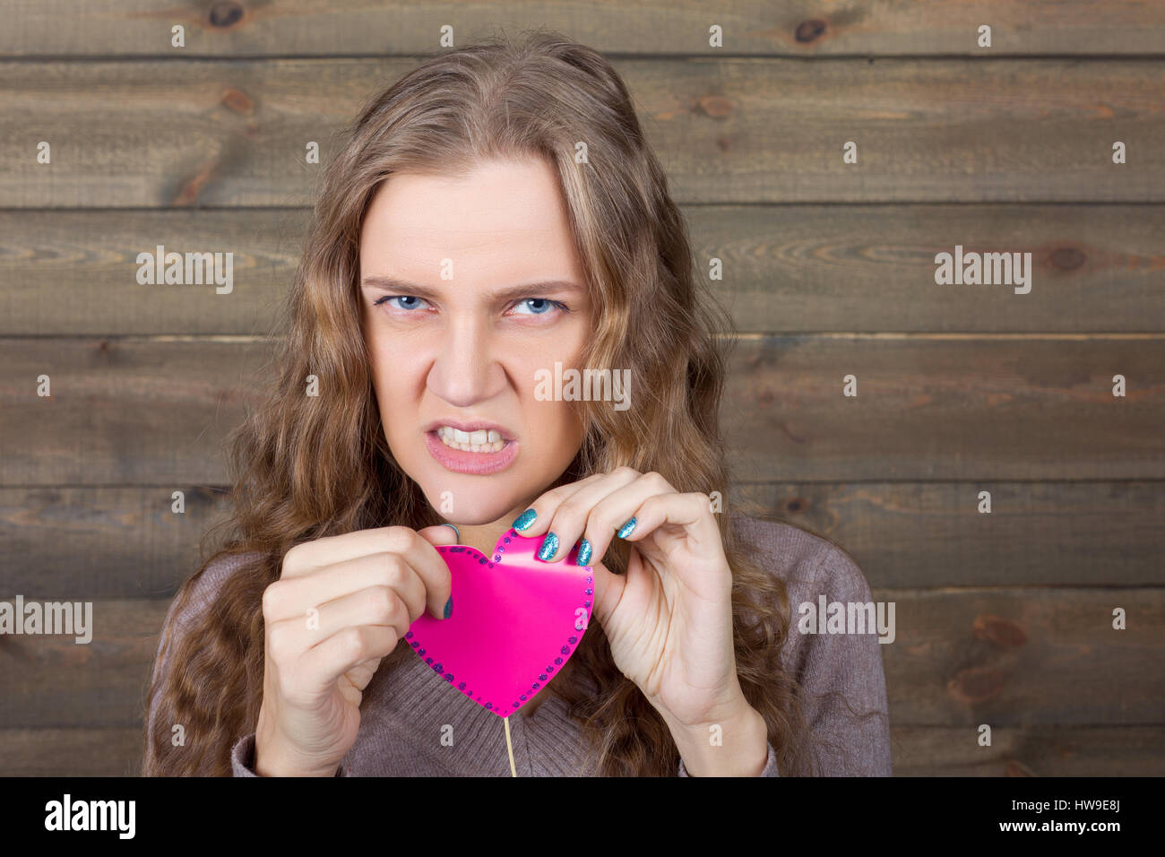 Young girl with angry face holding pink heart on a stick in her hands ...