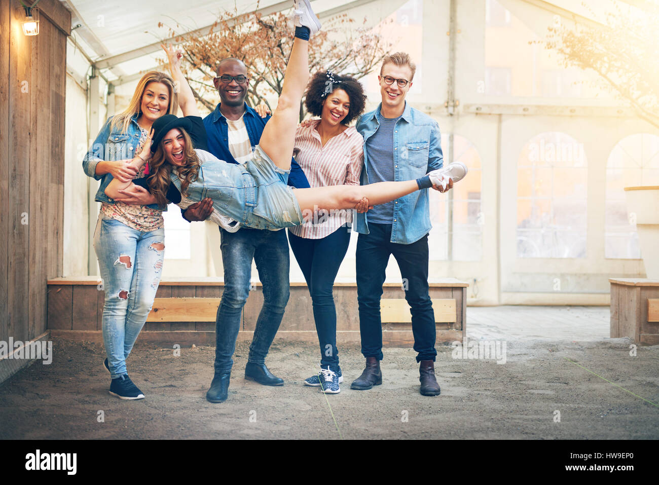 Several beautiful young people lifting their friend girl in hat to pose ...