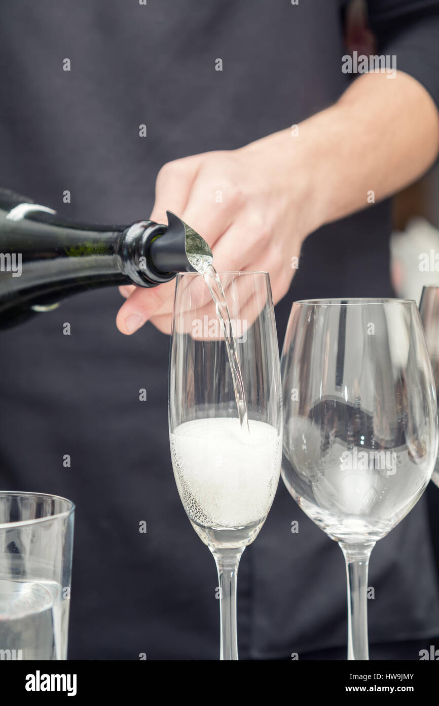 Sommelier pouring sparkling wine to the wine glass. Serving table ...