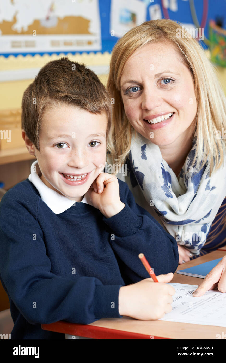 Teacher Helping Male Elementary Pupil Working At Desk Stock Photo - Alamy