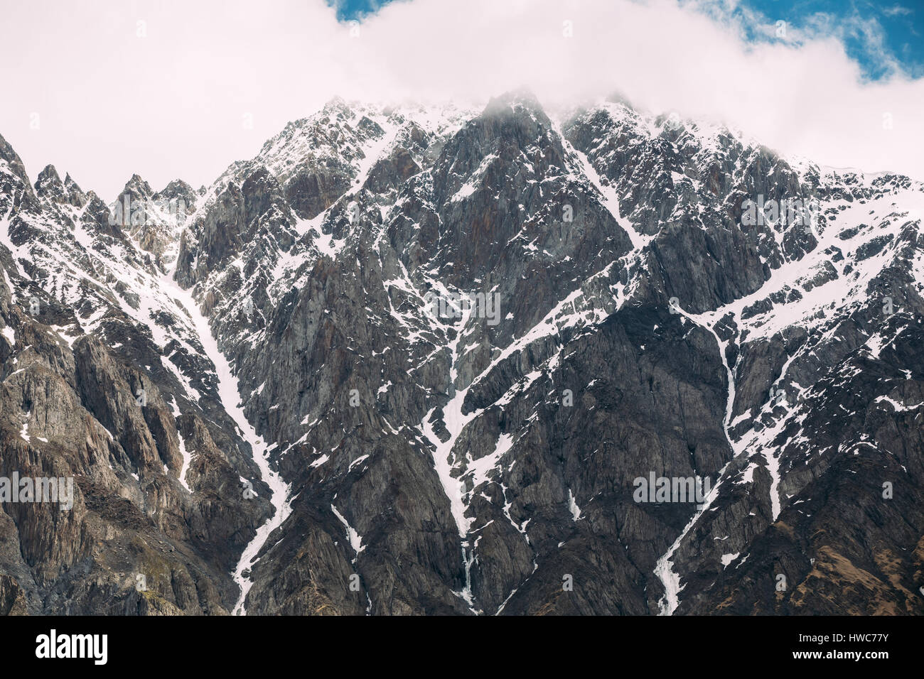 Clouds fly low over rocks. Mountain peaks covered with snow. Varied ...