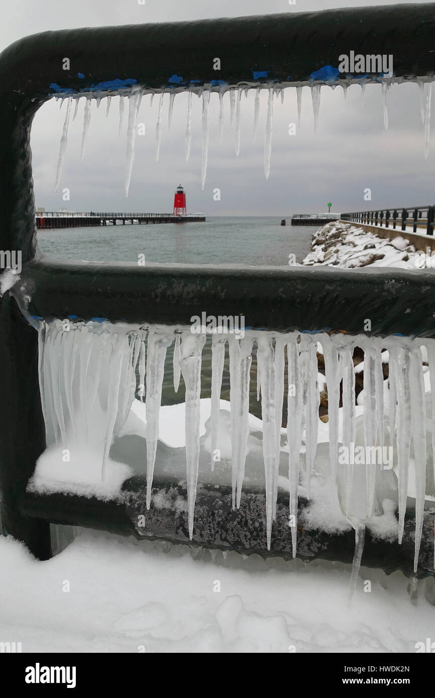 Looking through an icicle filled railing at a red lighthouse on an ...