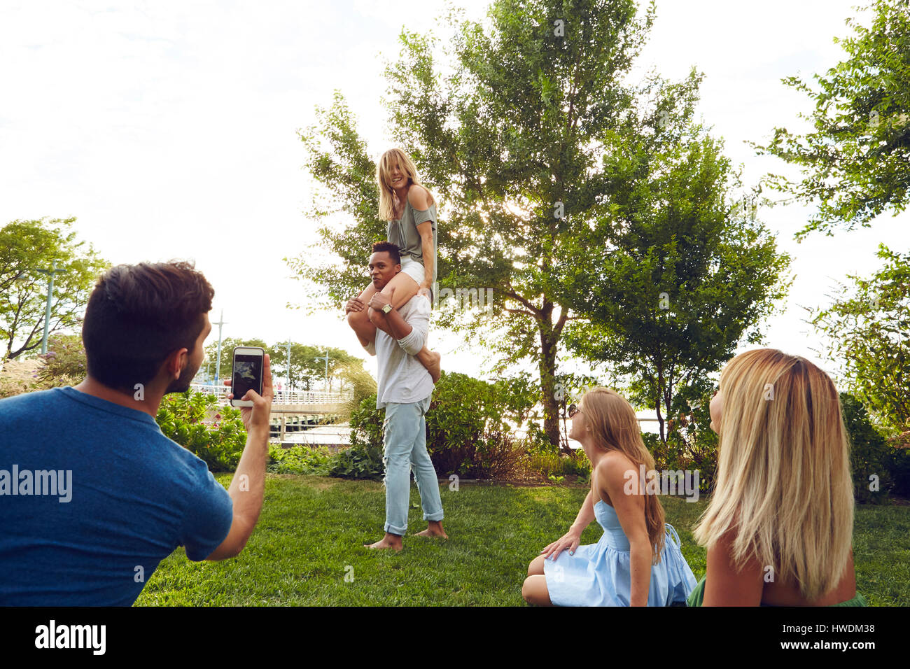 Young man photographing shoulder carrying friends in park Stock Photo ...
