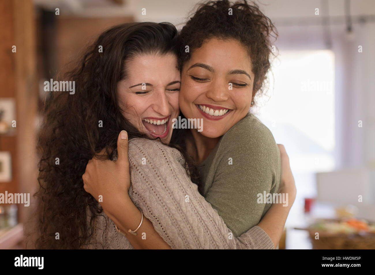 Two young women friends hugging in kitchen Stock Photo - Alamy