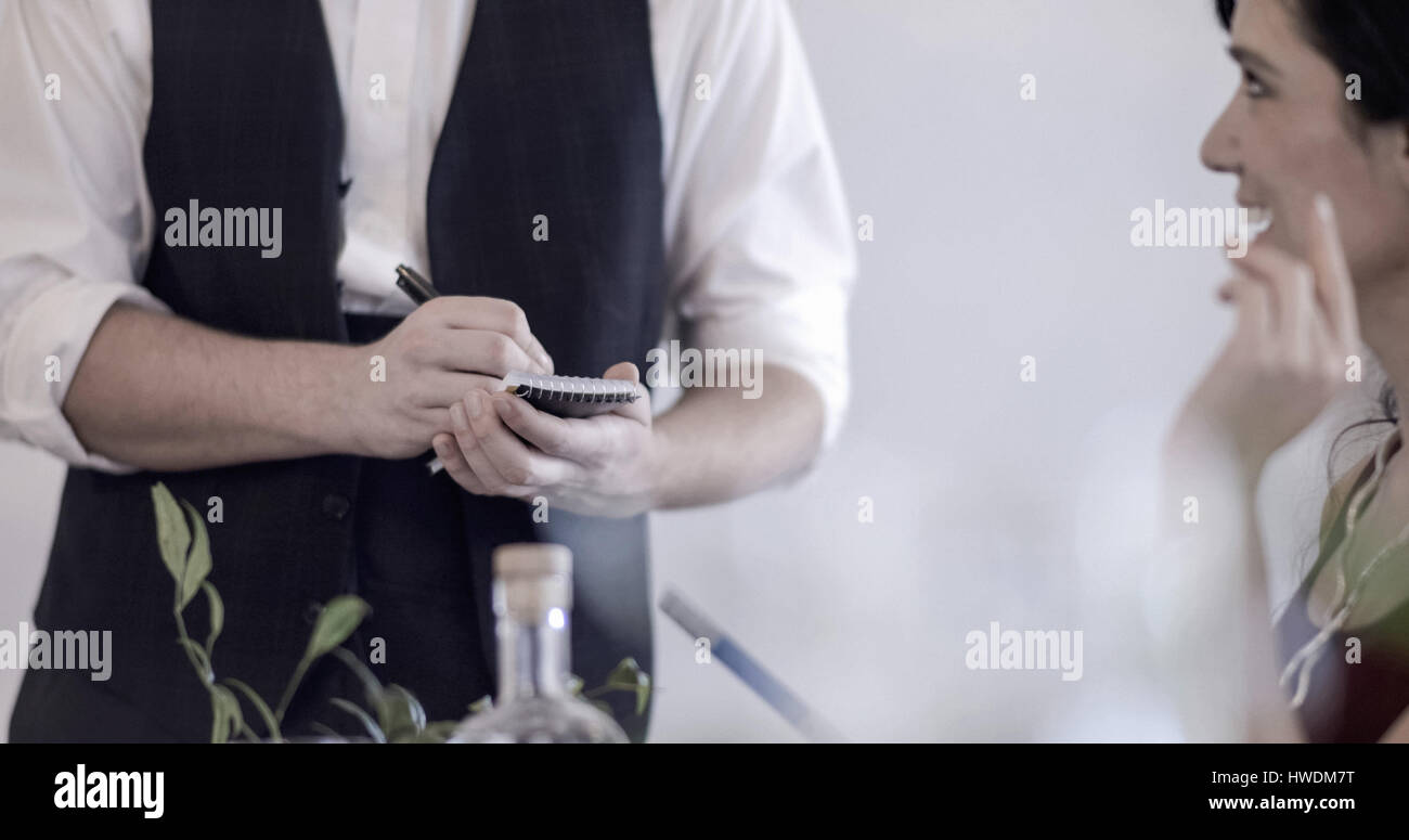 Waiter serving diner in restaurant, using pen and notepad, mid section ...