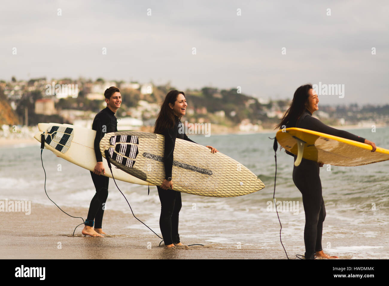 Three friends standing in sea, holding surfboards, preparing to surf ...