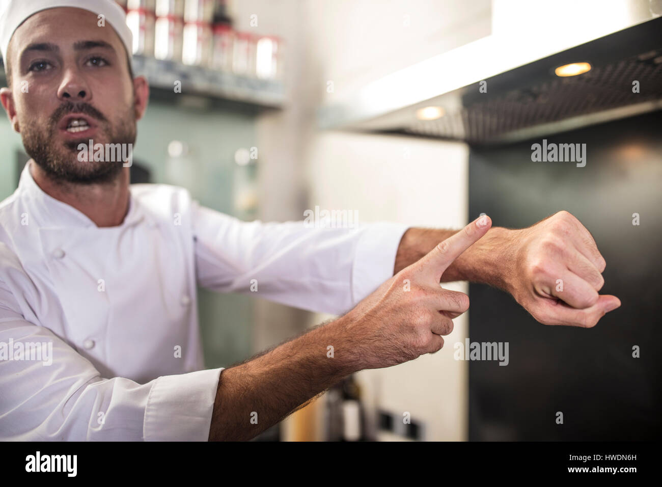 Chef signalling time by putting finger on wrist Stock Photo - Alamy