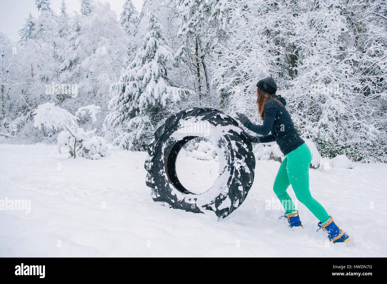 Woman rolling tire through snow Stock Photo - Alamy