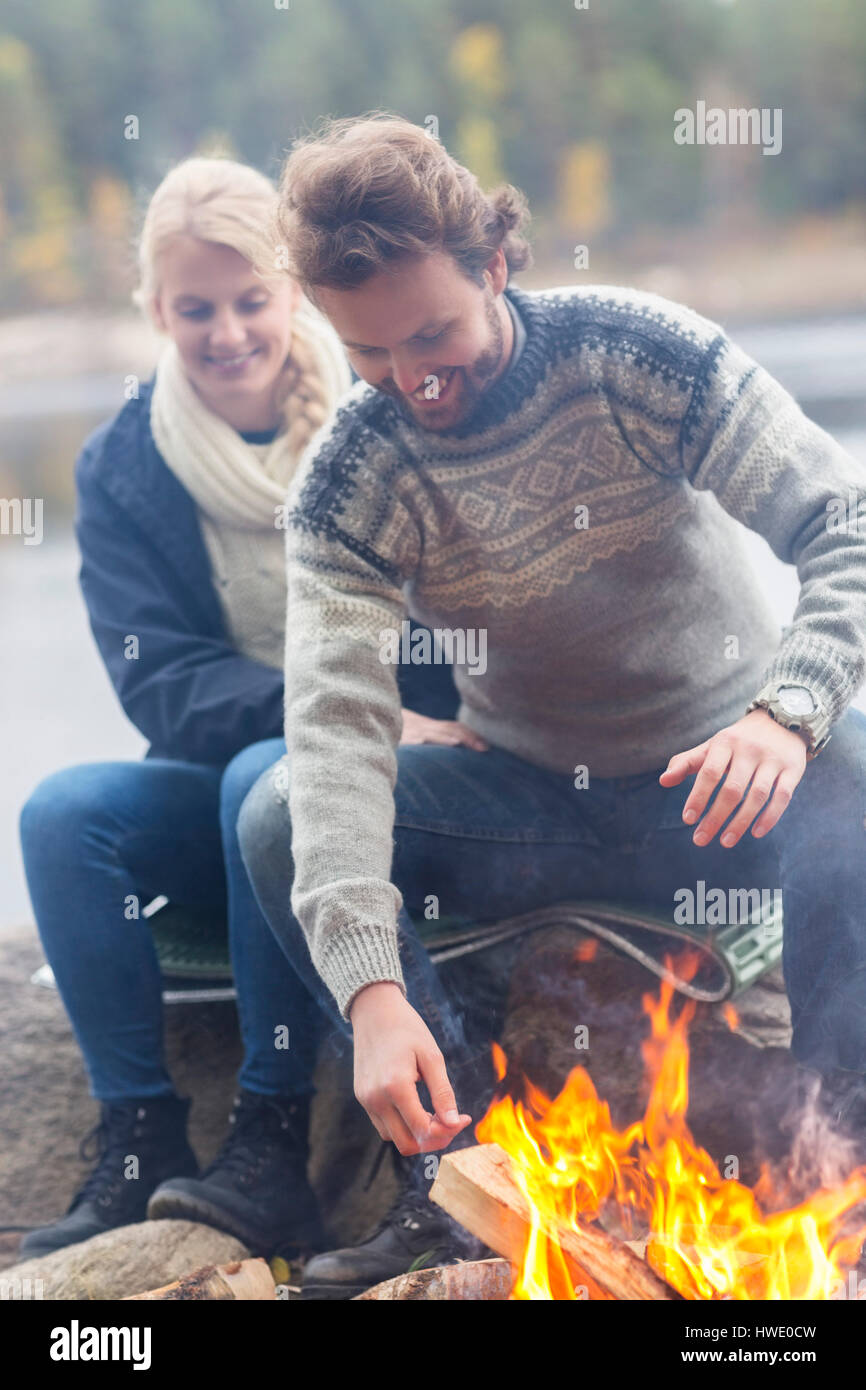 Happy Couple Sitting By Bonfire On Lakeshore Stock Photo - Alamy