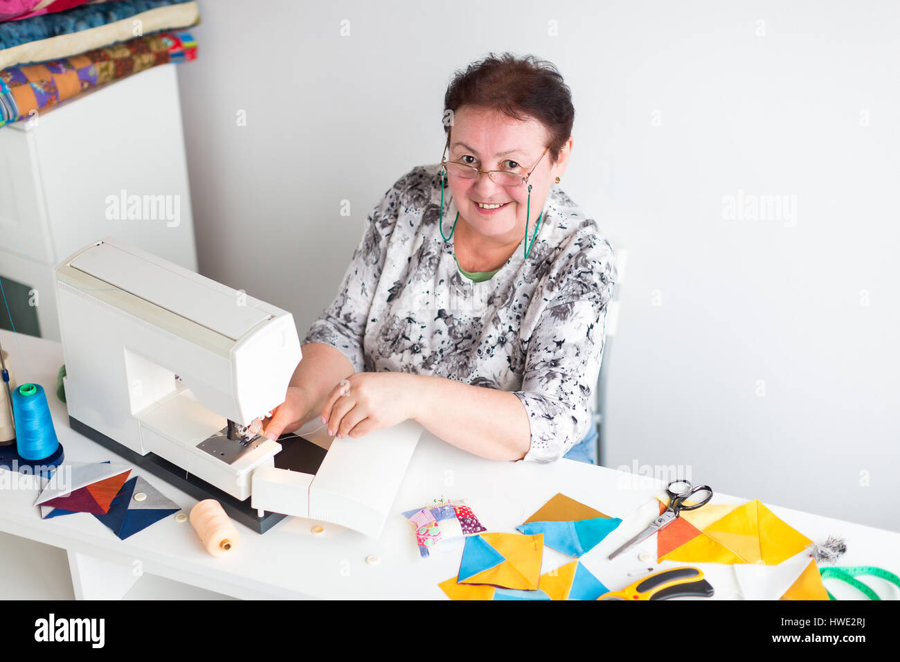 the smiling woman with eyeglasses working on sewing machine in atelier ...
