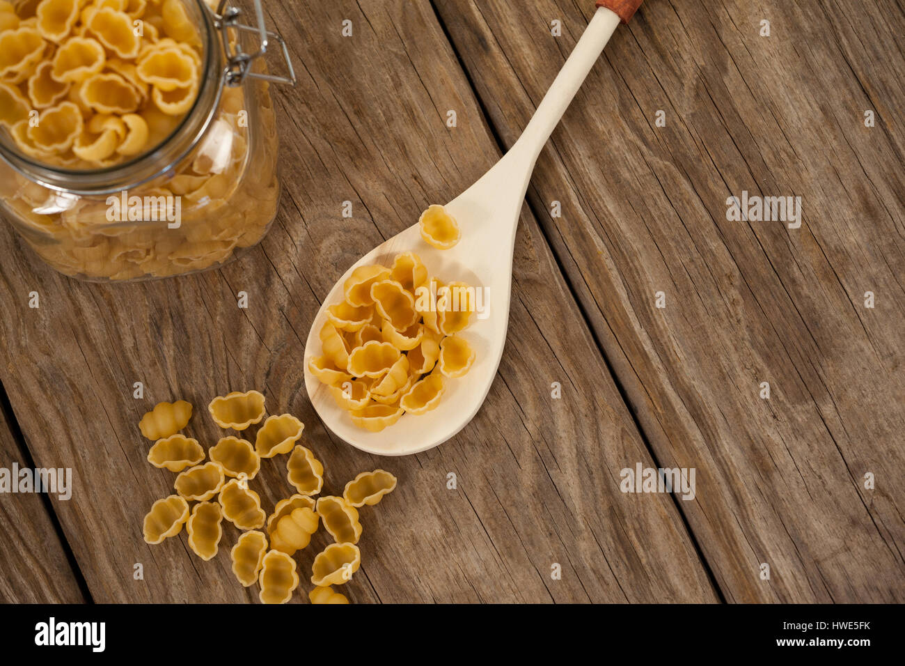 Conchiglie pasta spilling out of jar and spoon on wooden table Stock ...