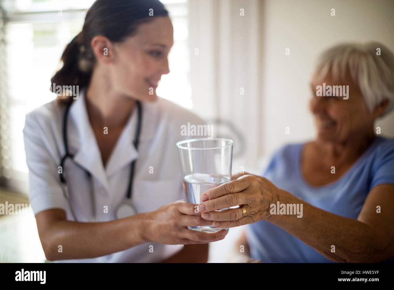 Female doctor serving a water glass to senior woman in the bedroom at ...