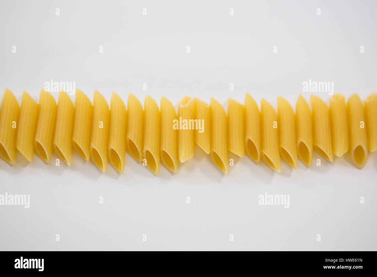 Pennette pasta arranged in a row on white background Stock Photo - Alamy