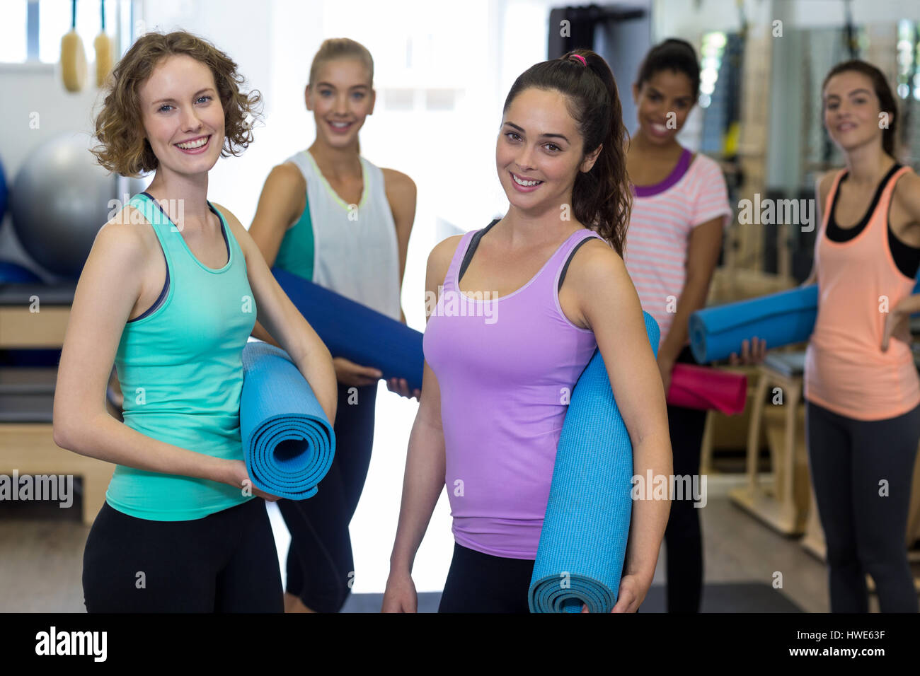 Portrait of beautiful women holding yoga mat in gym Stock Photo - Alamy