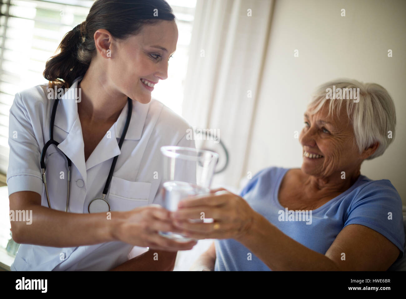 Female doctor serving a water glass to senior woman in the bedroom at ...
