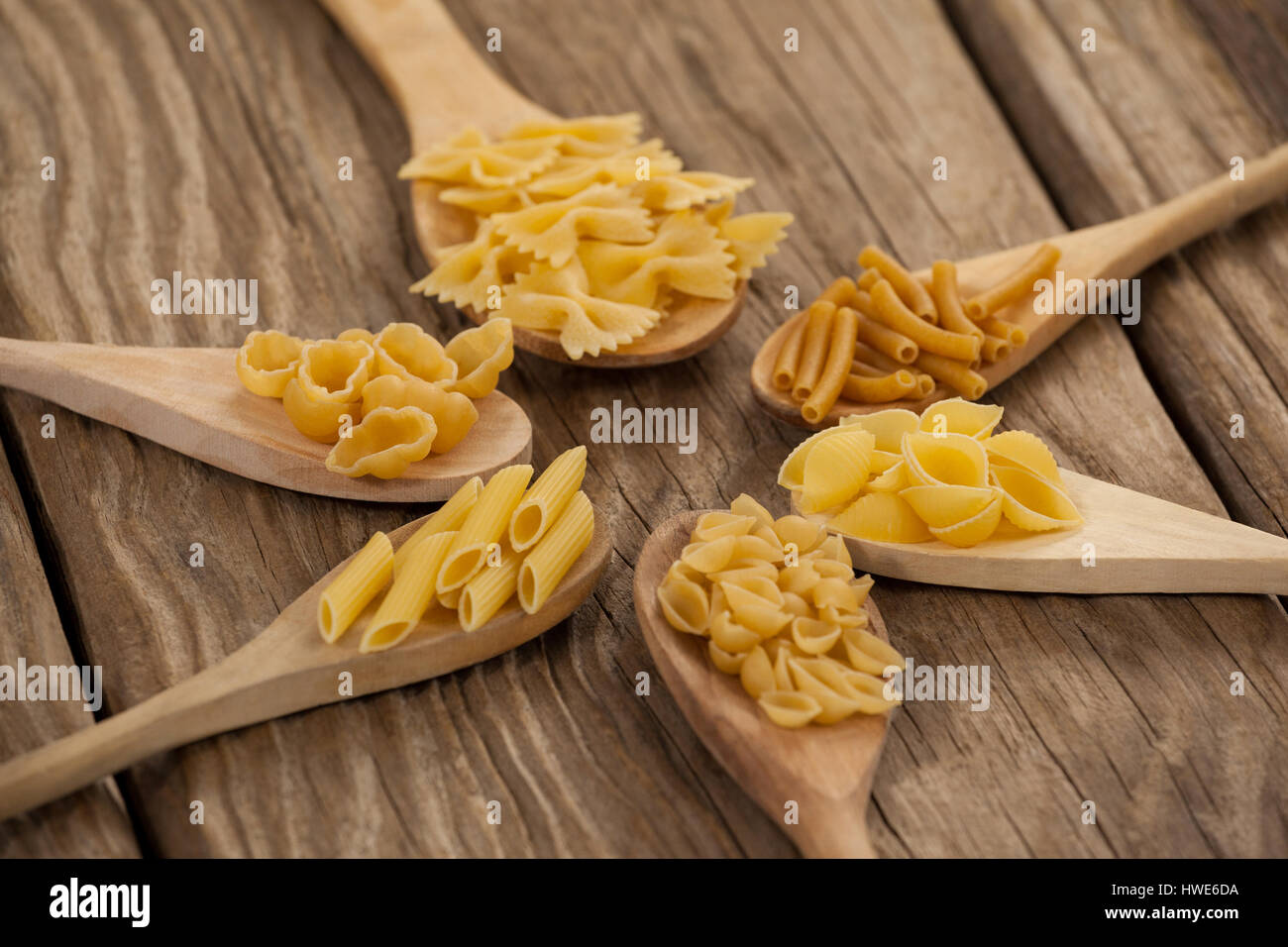 Spoons filled with varieties of pasta on wooden background Stock Photo ...