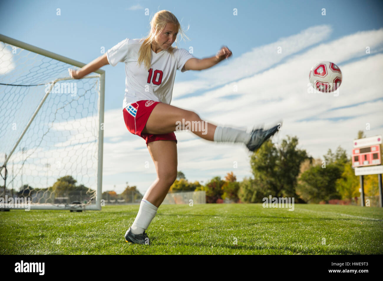 Low angle view of athlete kicking soccer ball on field under blue sky ...