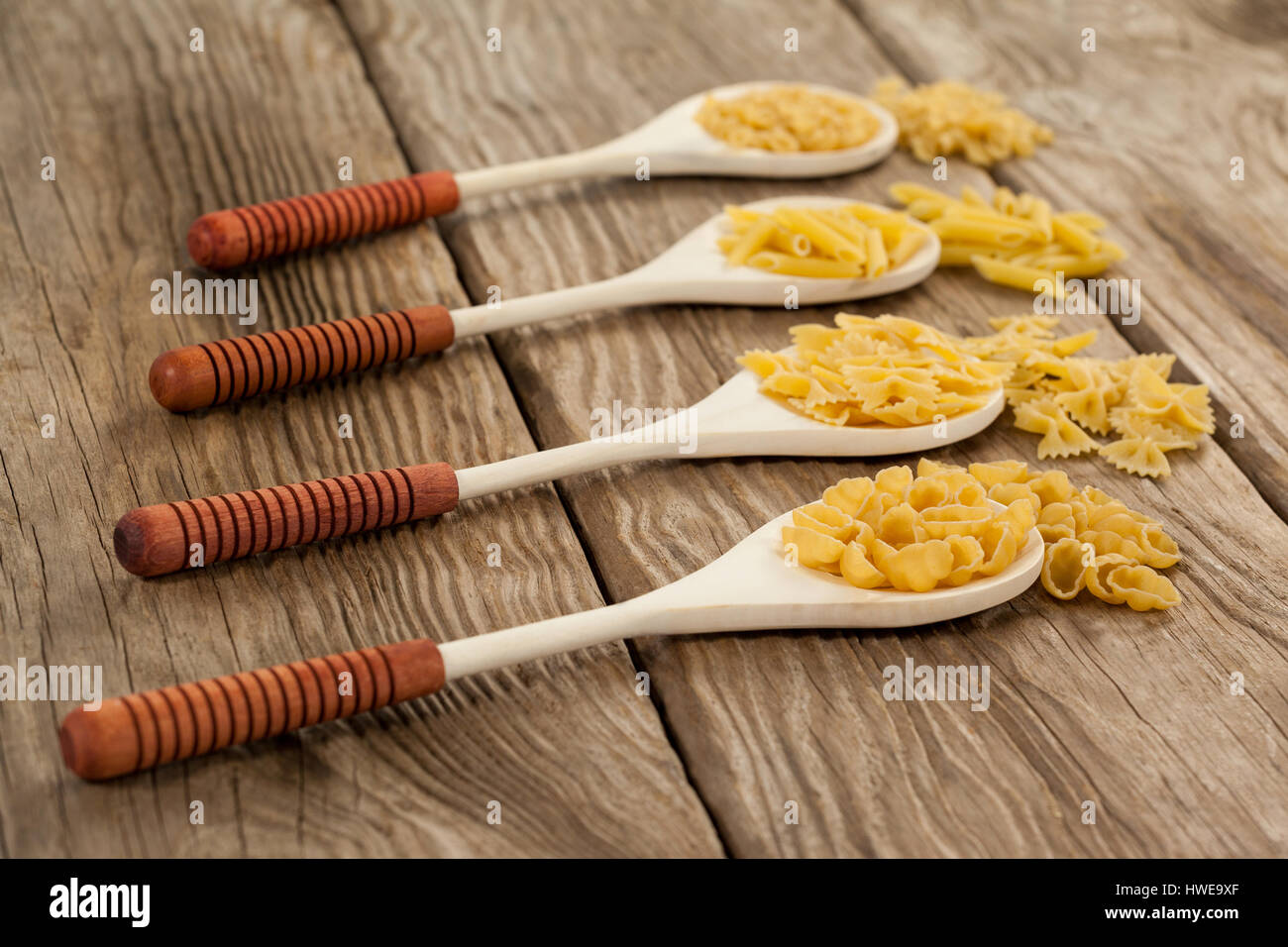 Spoons filled with varieties of pasta on wooden background Stock Photo ...