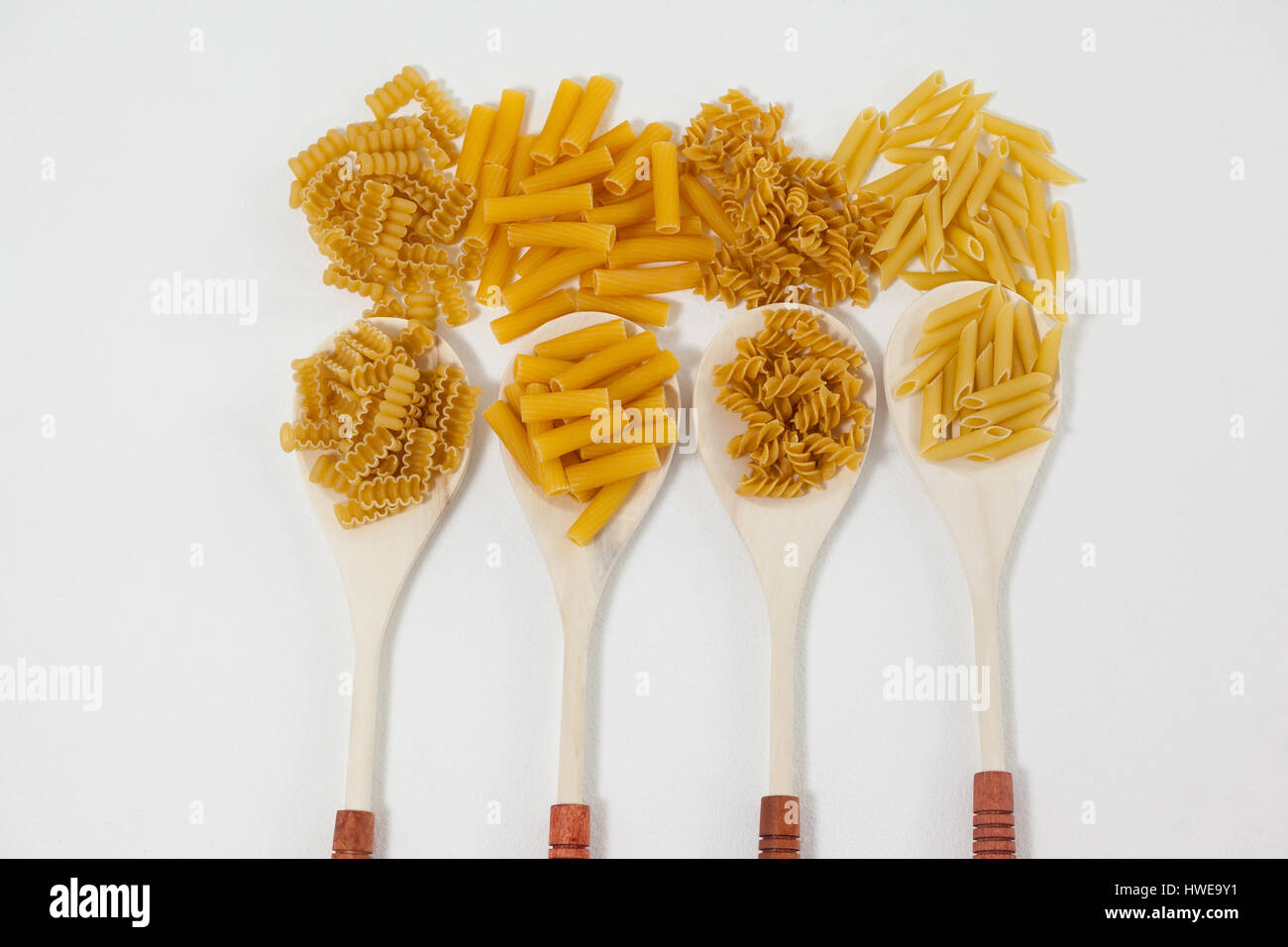 Varieties of pasta spilling out of spoons on white background Stock ...