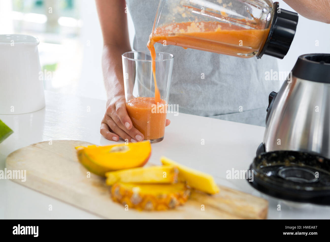 Woman pouring smoothie into glass at counter in kitchen Stock Photo - Alamy