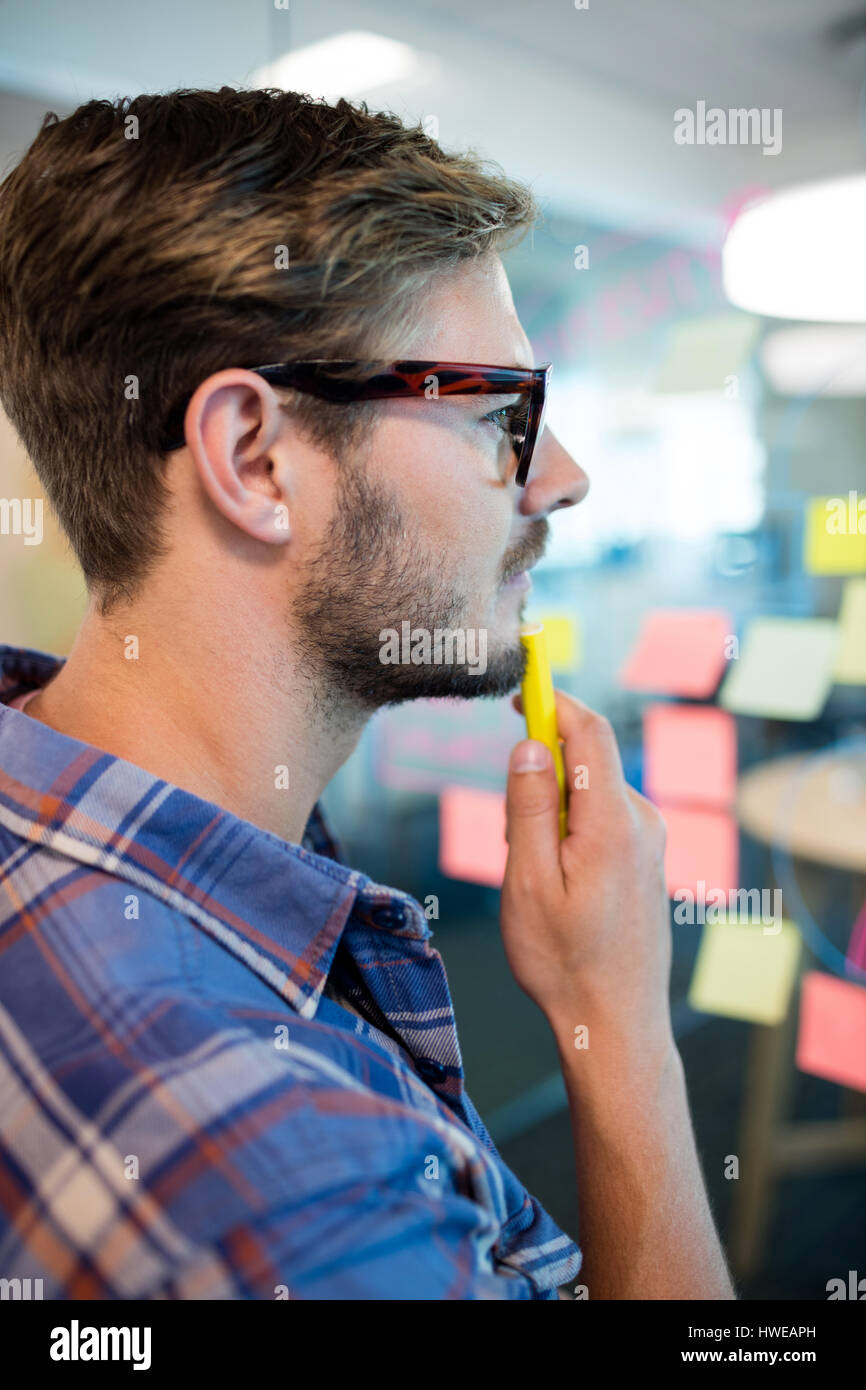 Thoughtful man reading sticky notes on the glass wall in office Stock ...