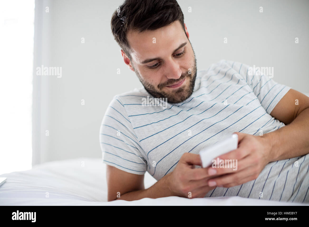 Man using mobile phone on bed in bedroom Stock Photo - Alamy