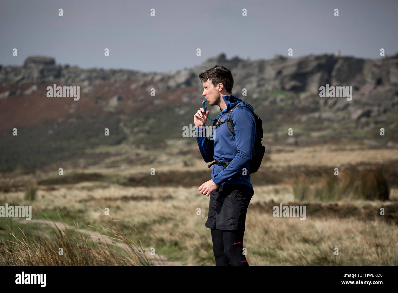 Male runner drinking from tube at Stanage Edge, Peak District ...