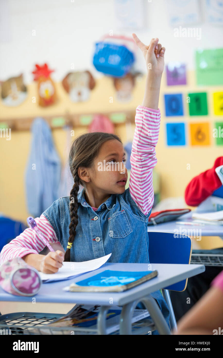Primary schoolgirl with hand raised in classroom Stock Photo - Alamy