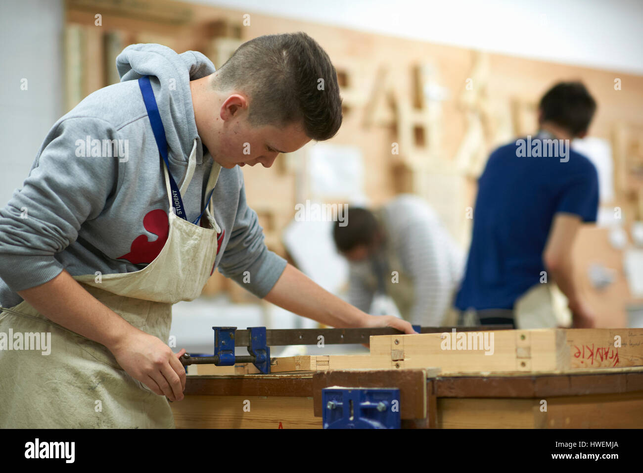 Male teenage carpentry student adjusting wood clamp in college workshop ...