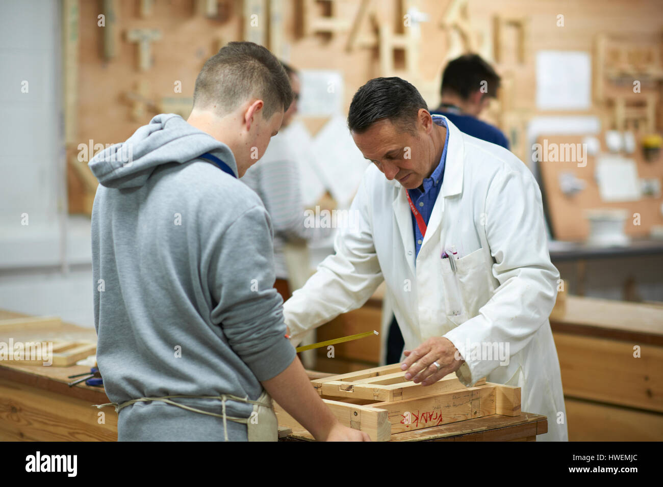 Male lecturer demonstrating measurement to teenage carpentry student in ...