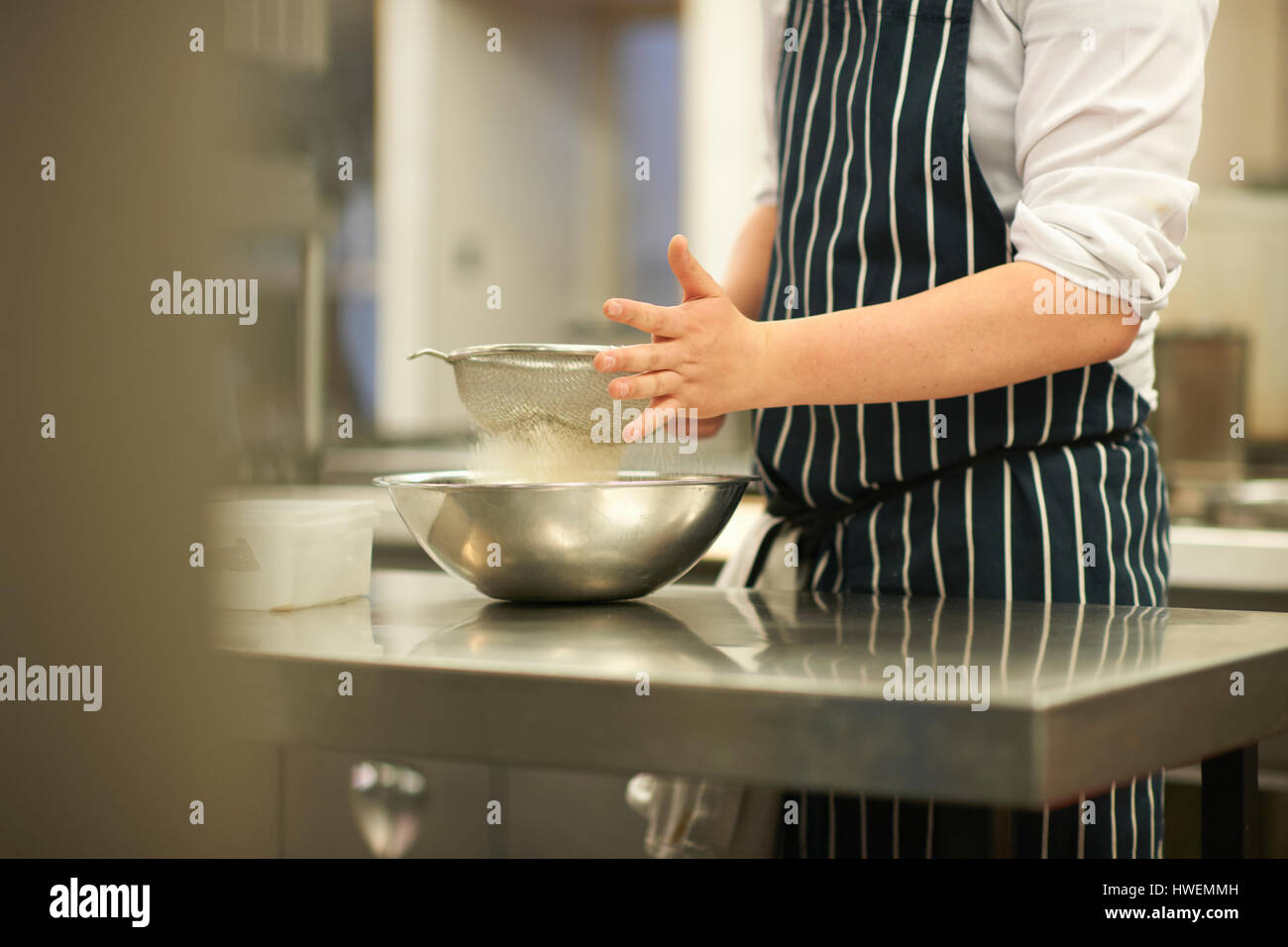 Mid section of male teenage catering student sifting flour into bowl at ...