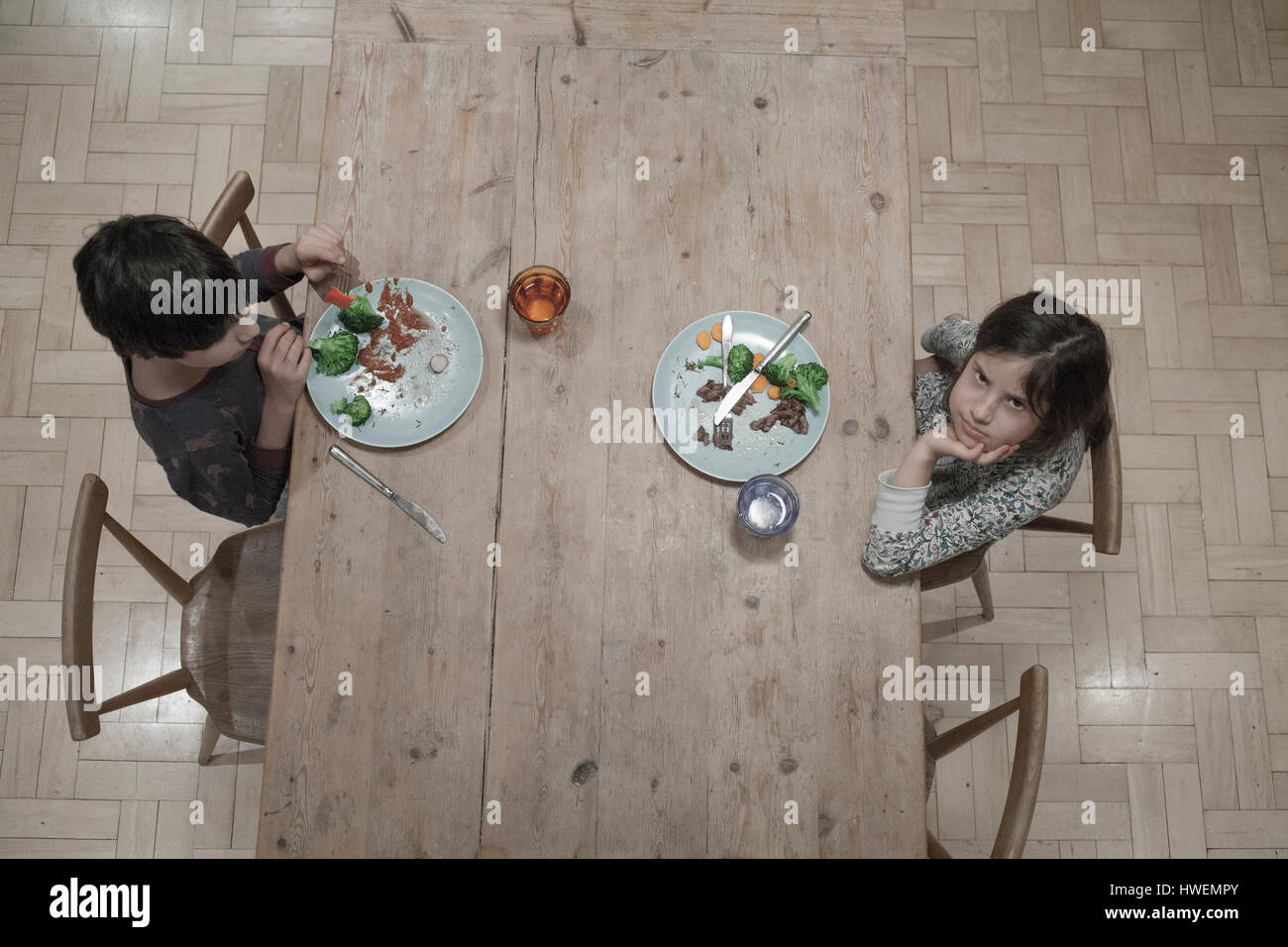 Overhead portrait of girl and brother eating dinner at kitchen table ...